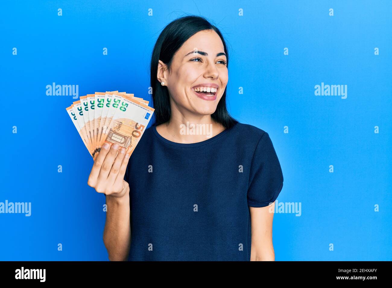 Beautiful young woman holding bunch of 50 euro banknotes looking away ...