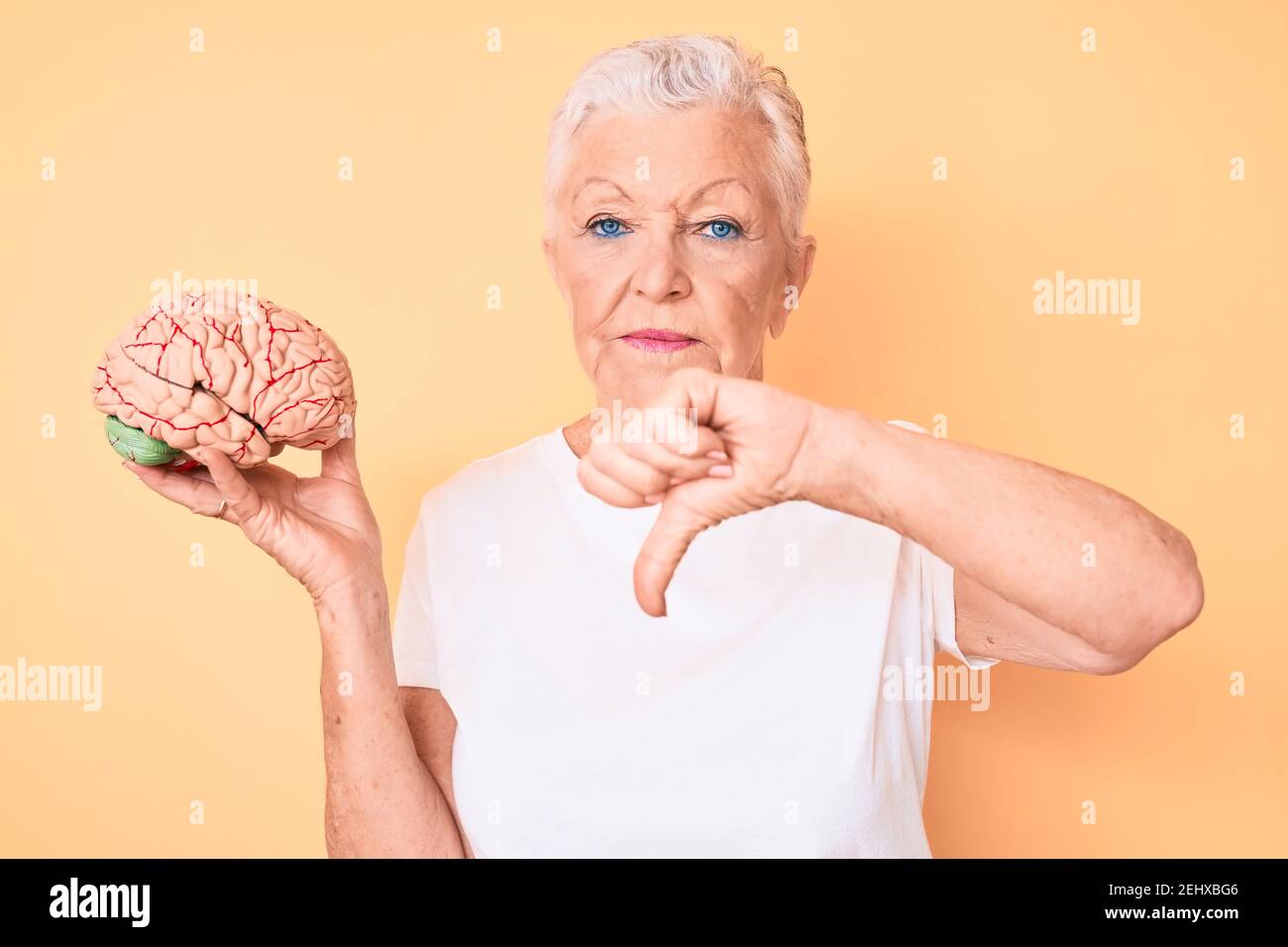 Senior beautiful woman with blue eyes and grey hair holding brain as ...
