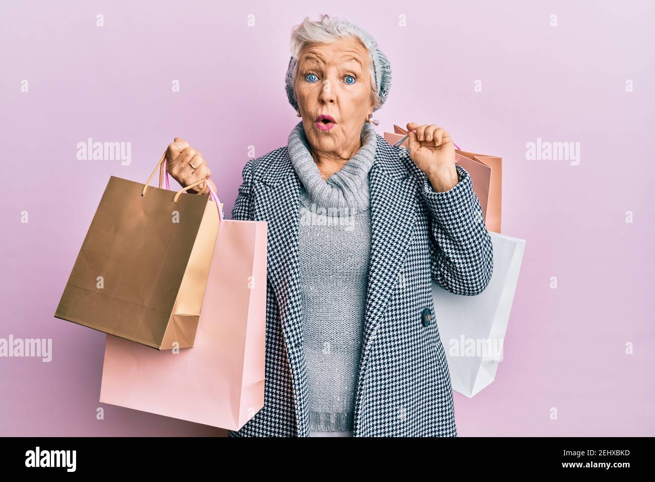 Senior grey-haired woman holding shopping bags in shock face, looking ...