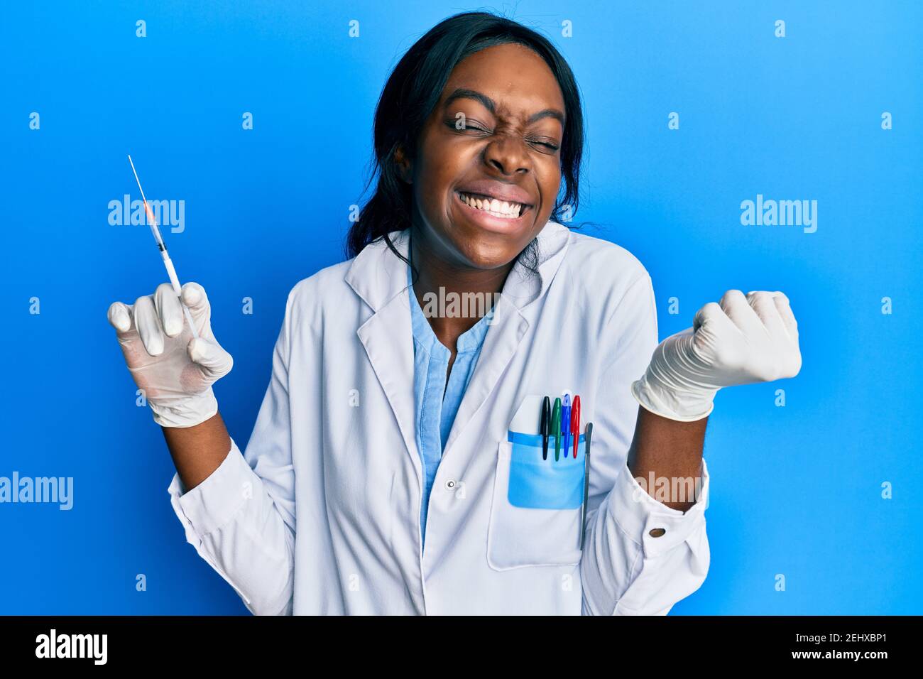 Young african american woman wearing scientist uniform holding syringe ...
