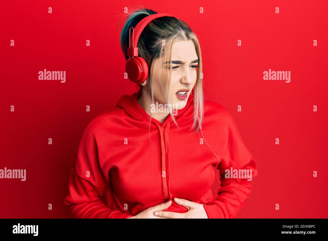 Young modern girl wearing gym clothes and using headphones with hand on ...
