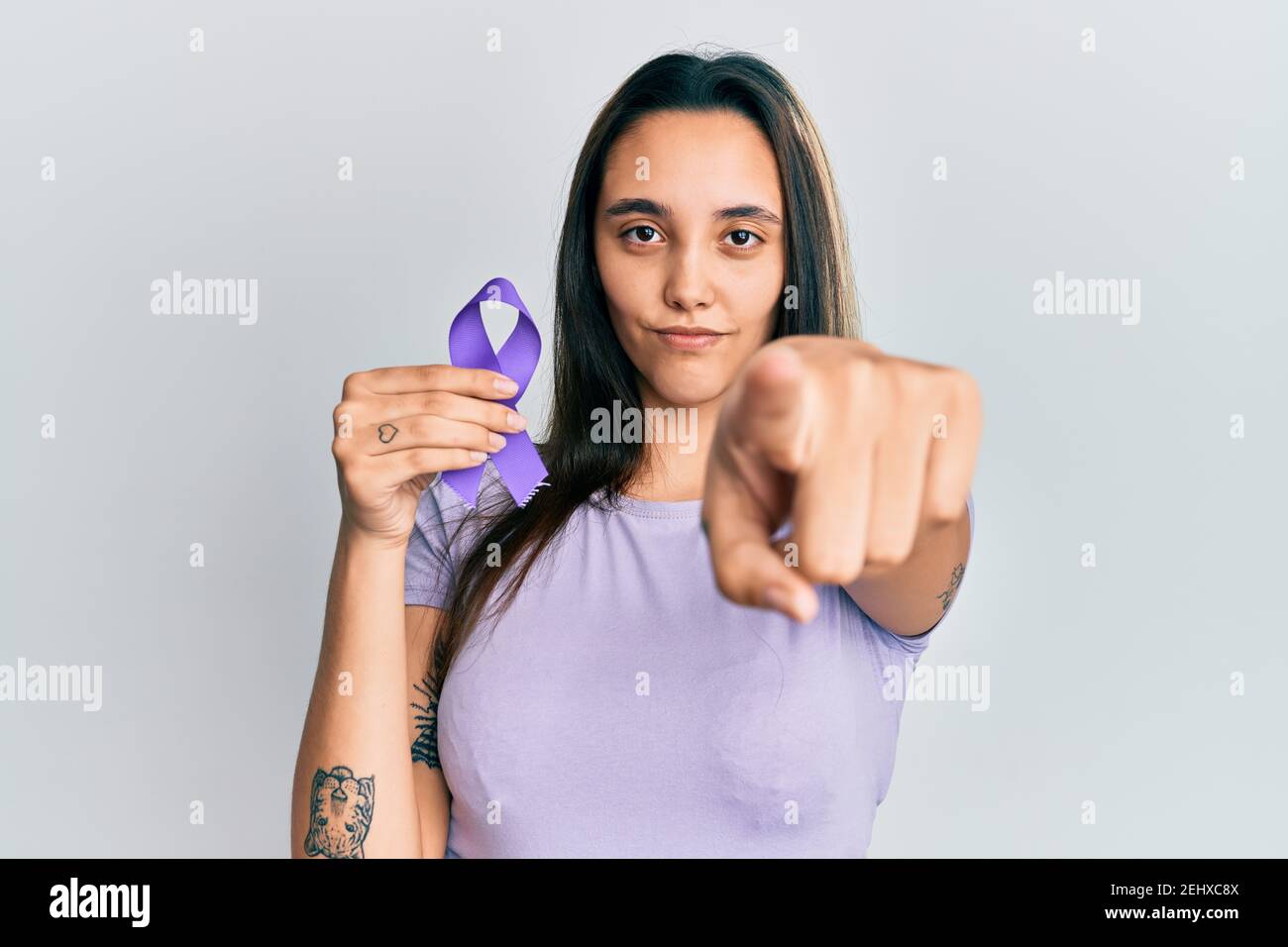 Young hispanic woman holding purple ribbon awareness pointing with ...