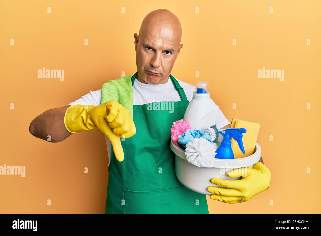 Middle age bald man wearing cleaner apron holding cleaning products ...
