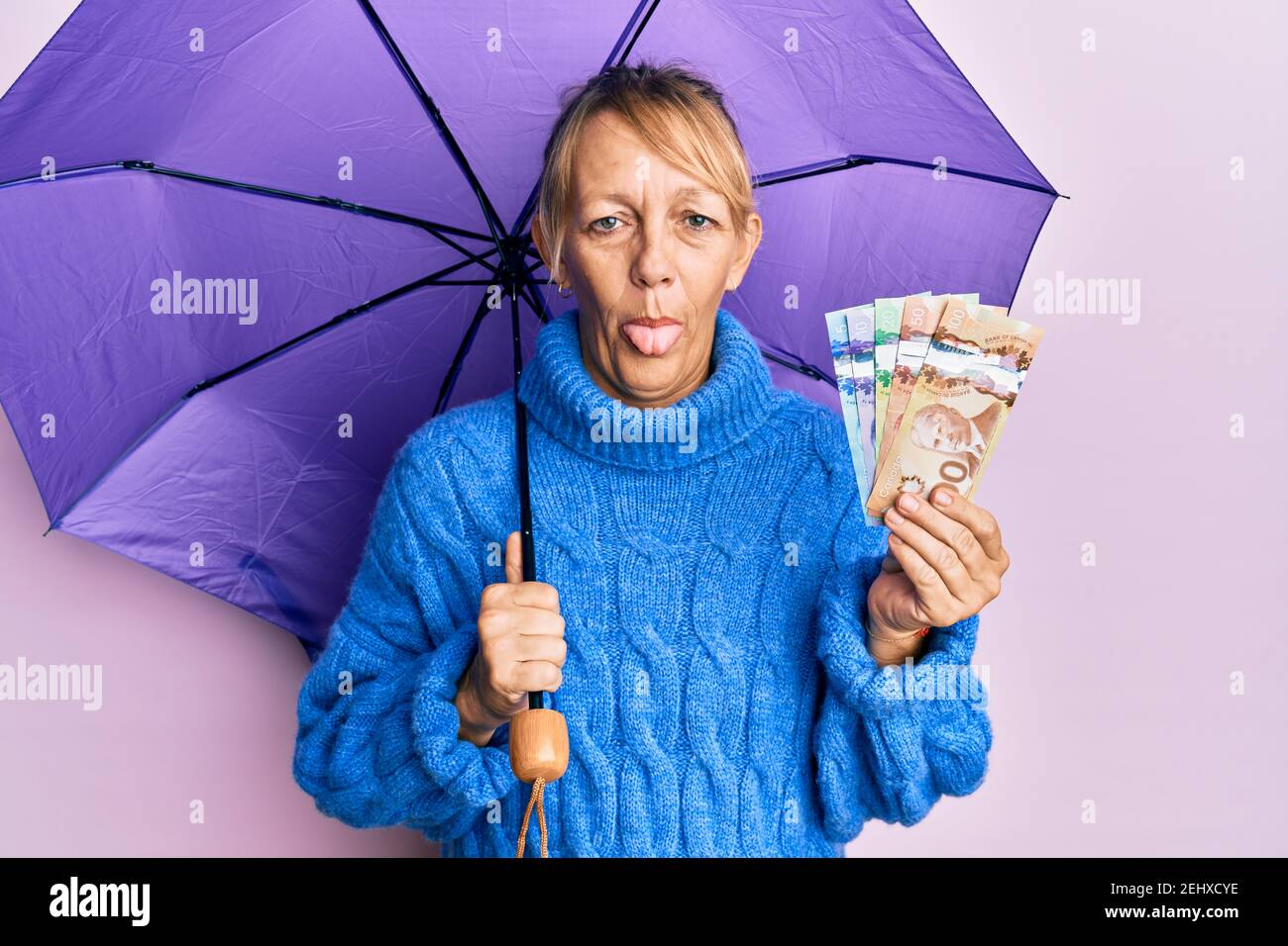 Middle age blonde woman holding umbrella and canadian dollars banknotes ...