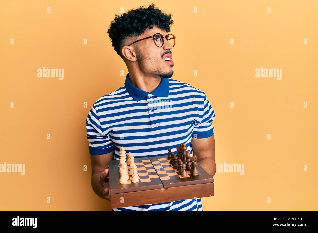 Young arab handsome man holding chess board wearing glasses angry and ...