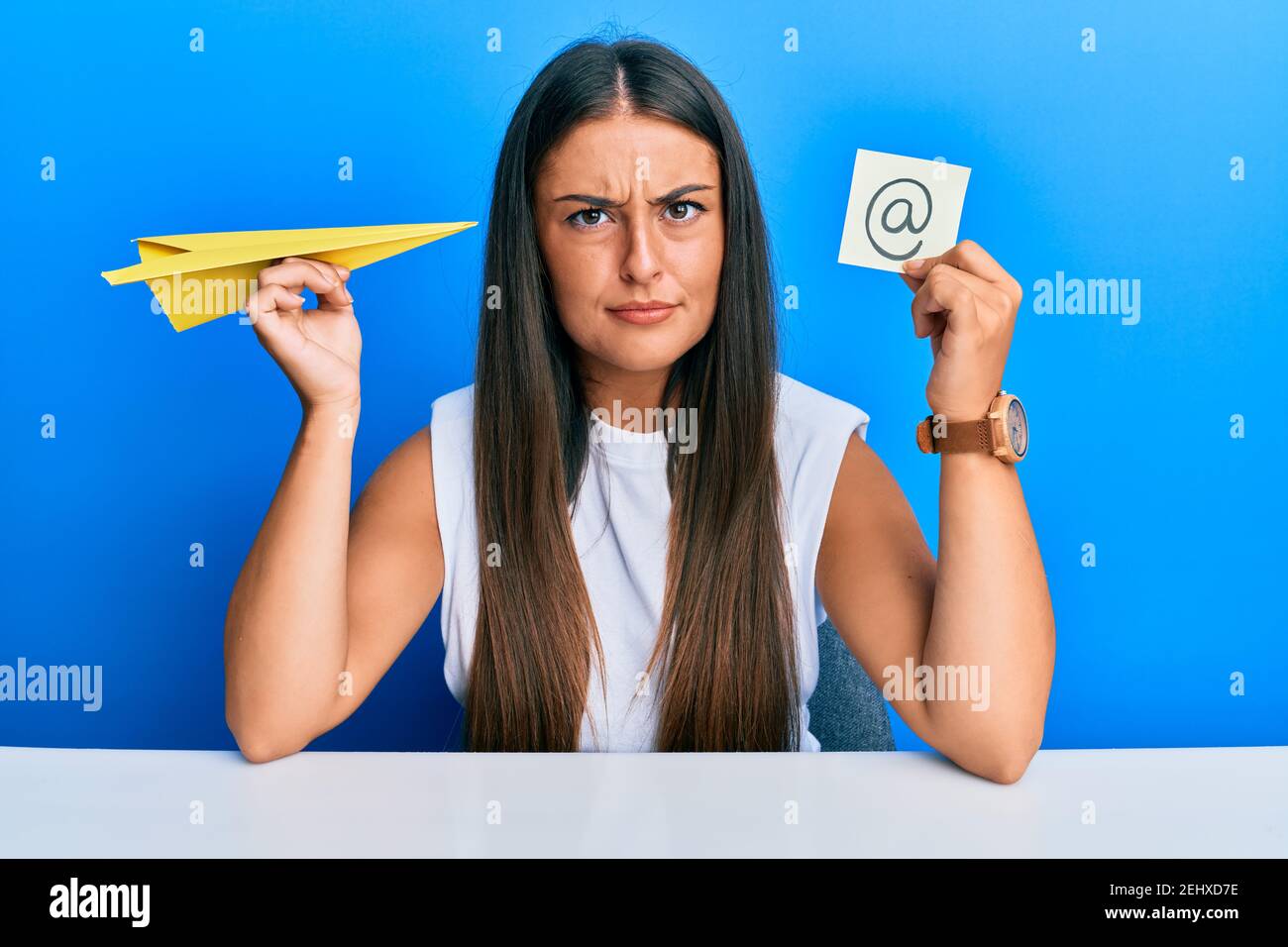 Beautiful hispanic woman holding paper plane and email symbol skeptic ...