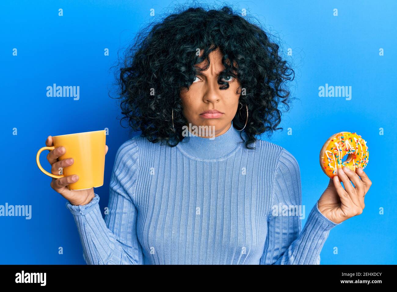 Young hispanic woman eating doughnut and drinking coffee depressed and ...