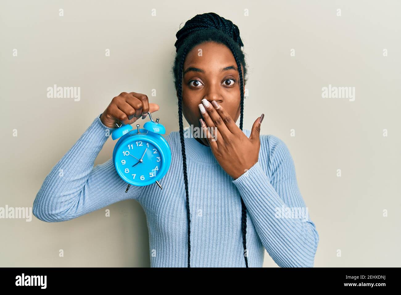 African american woman with braided hair holding alarm clock covering ...