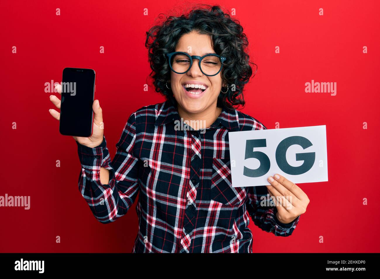 Young hispanic woman with curly hair holding 5g technology smartphone ...