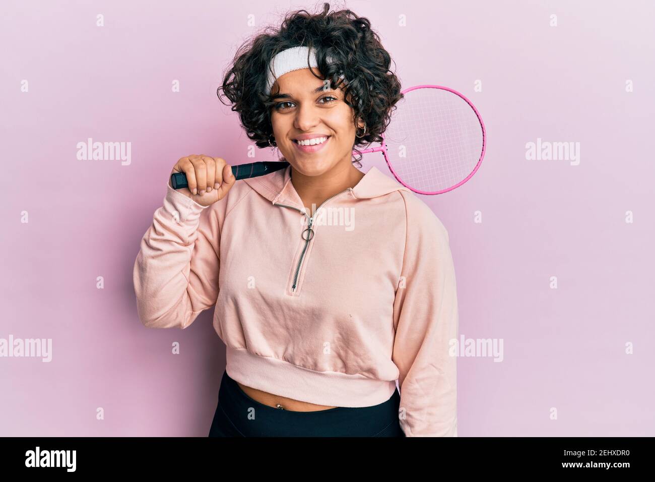 Young hispanic woman with curly hair holding badminton racket looking ...