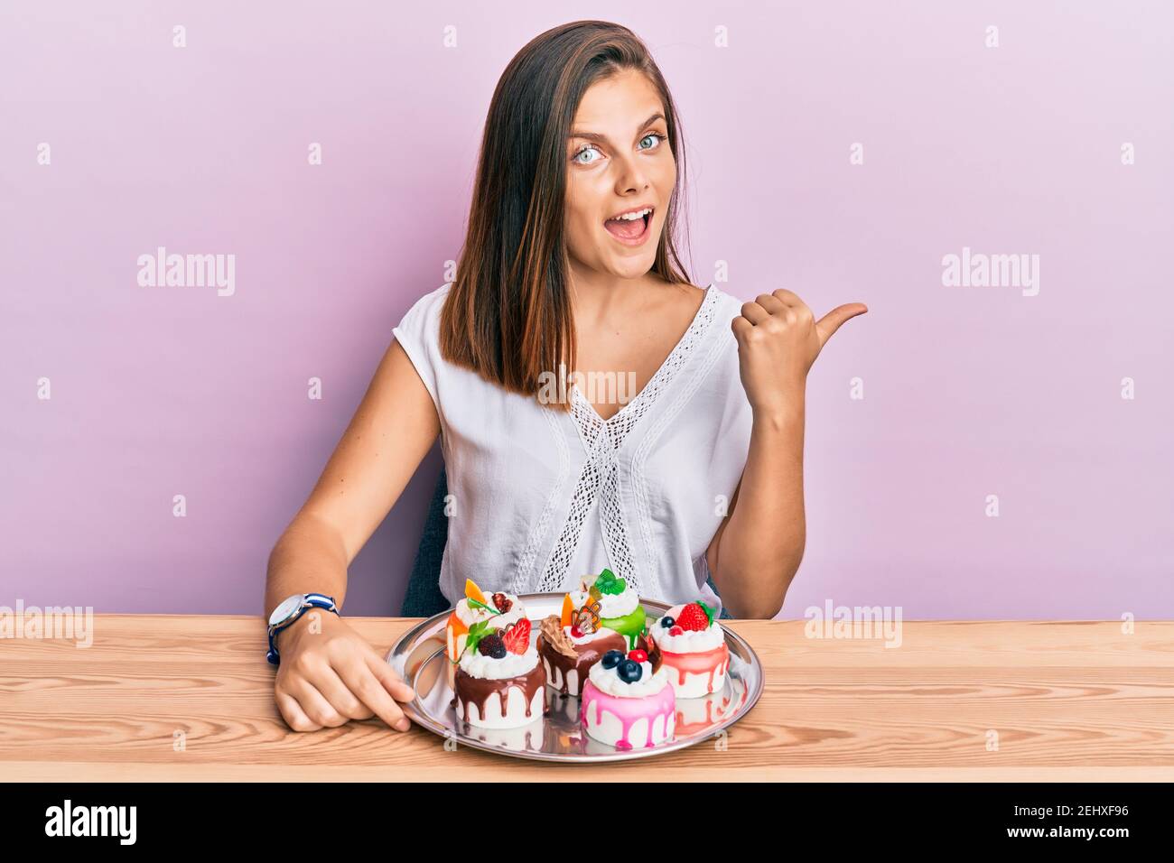 Young caucasian woman eating pastries for breakfast pointing thumb up ...