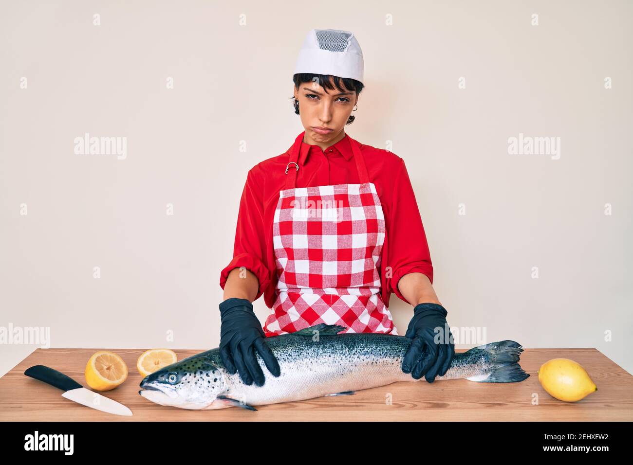 Beautiful brunettte woman fishmonger cooking fresh raw salmon depressed ...