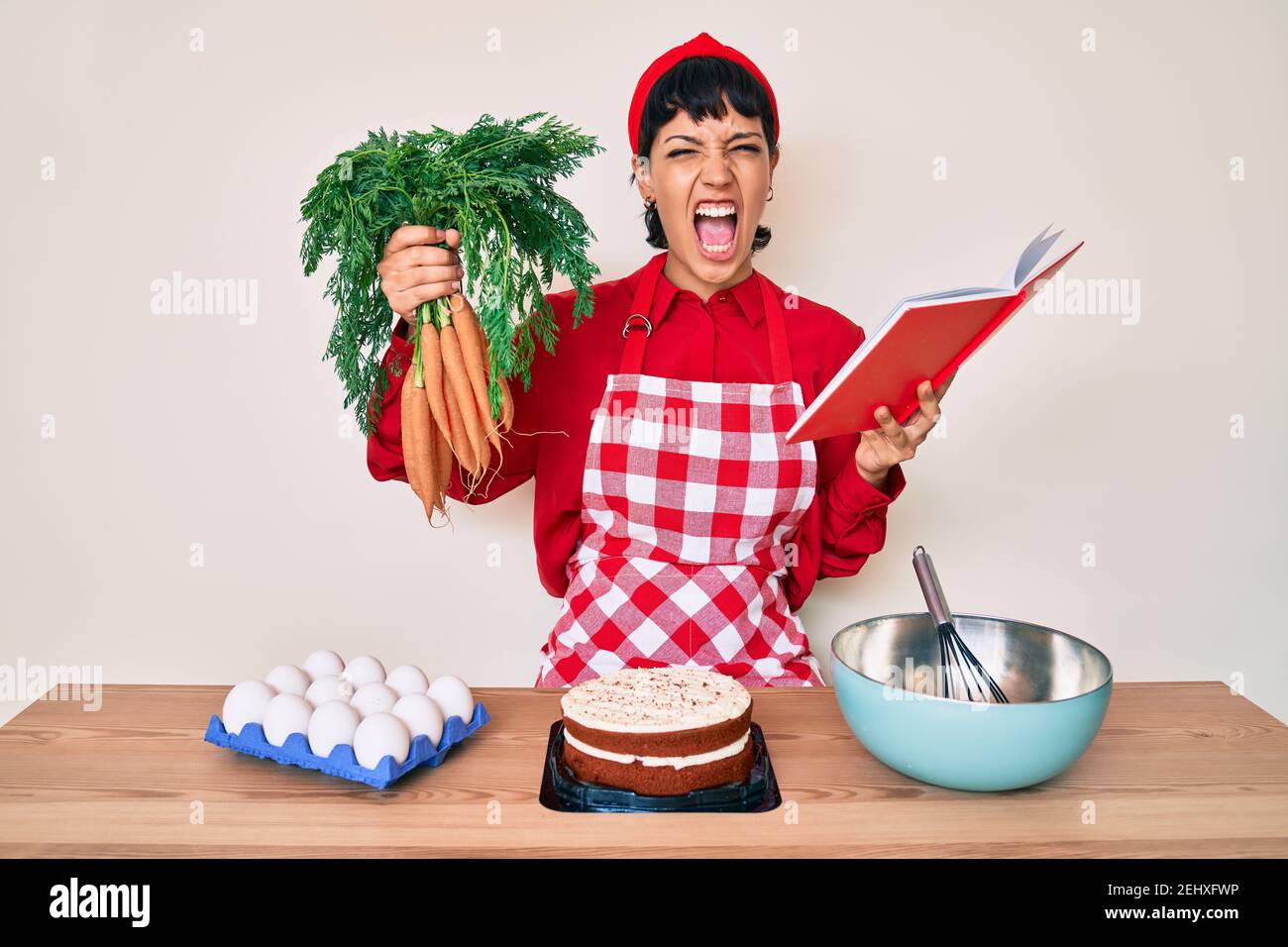 Beautiful brunettte woman cooking carrot cake reading recipes book ...