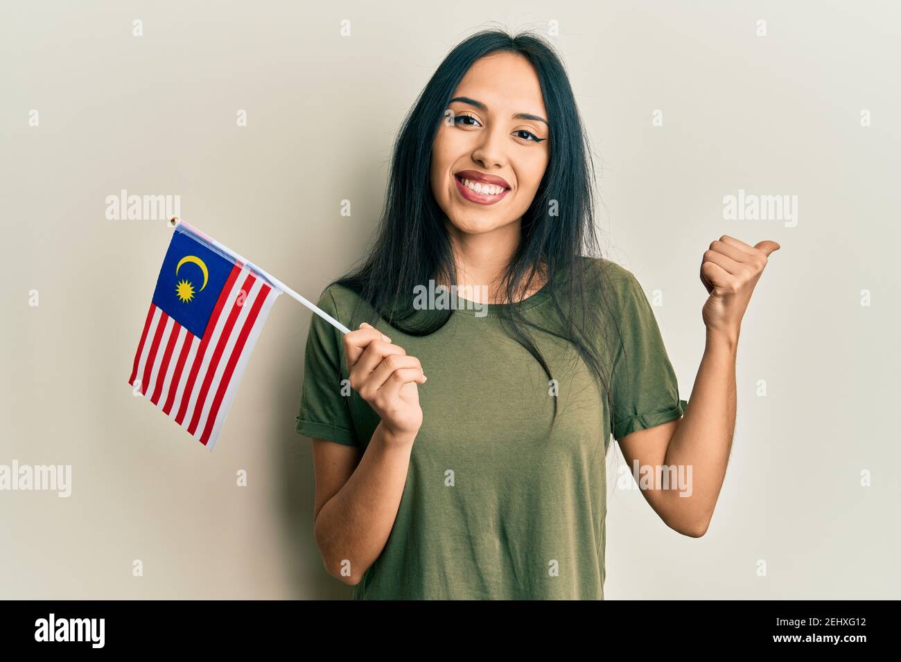 Young hispanic girl holding malaysia flag pointing thumb up to the side ...