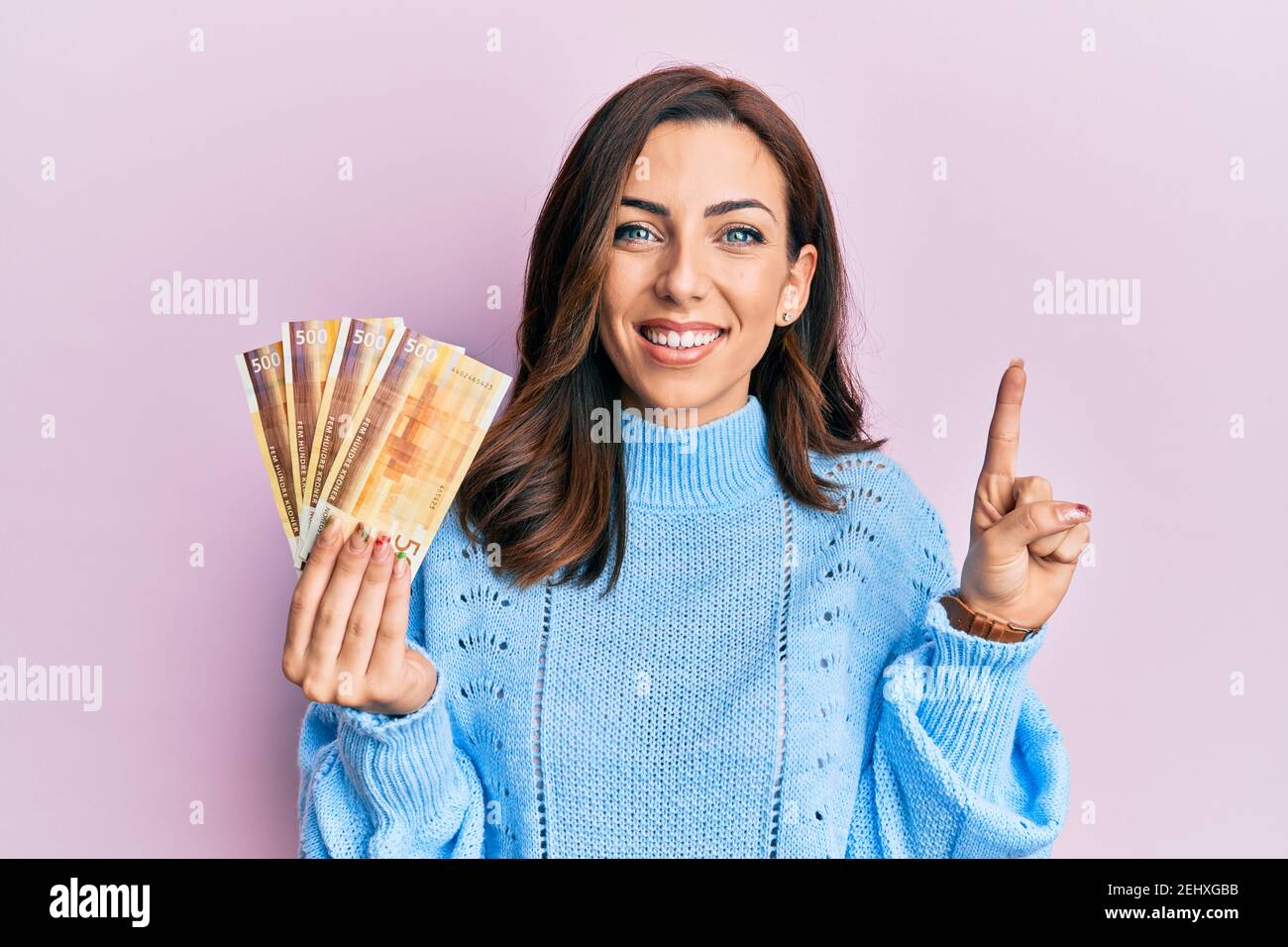Young brunette woman holding 500 norwegian krone banknotes smiling with ...