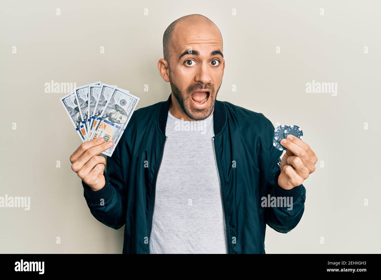 Young hispanic man playing poker holding dollars banknotes and chips ...