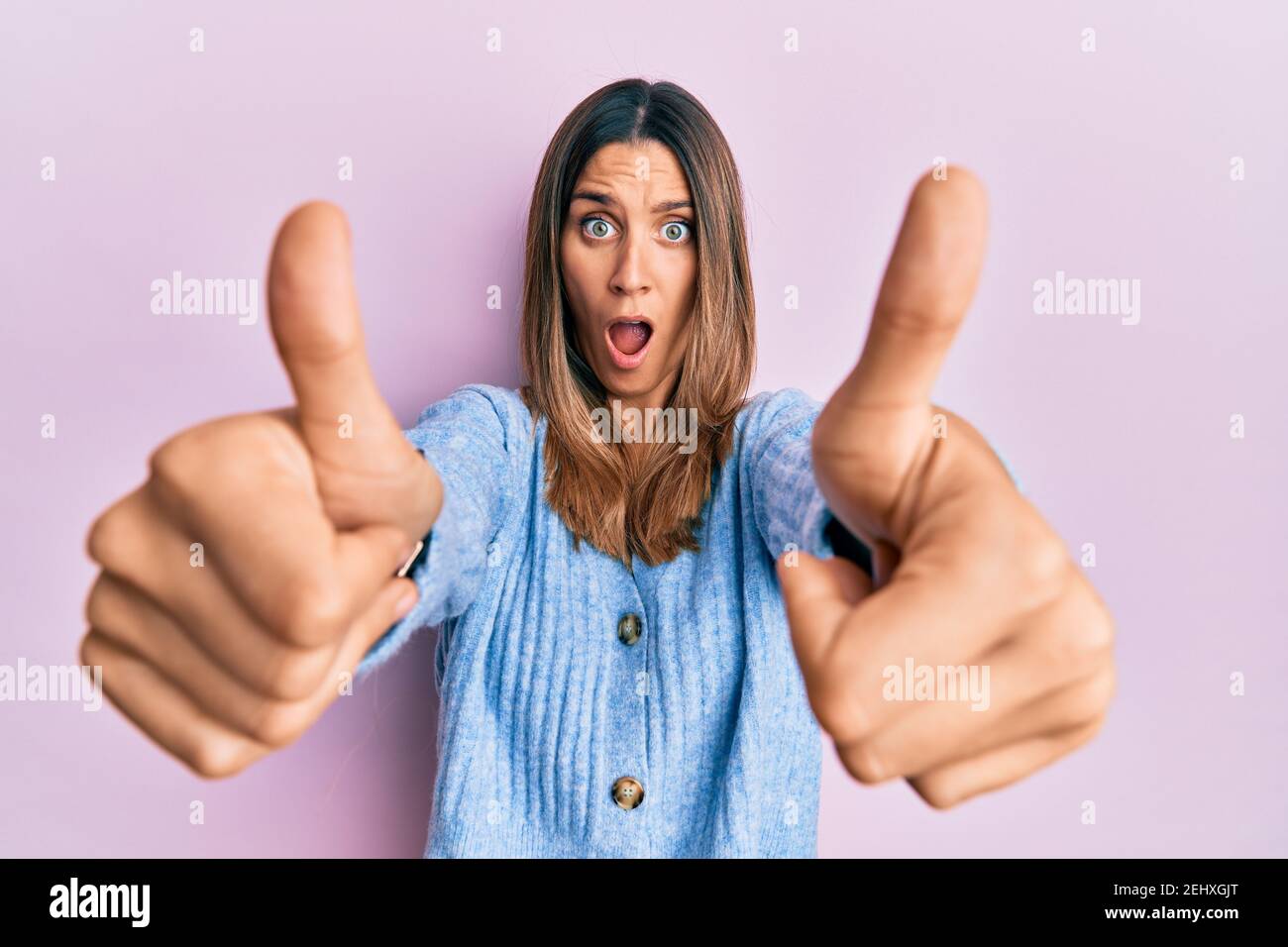 Brunette young woman doing thumbs up positive gesture afraid and ...