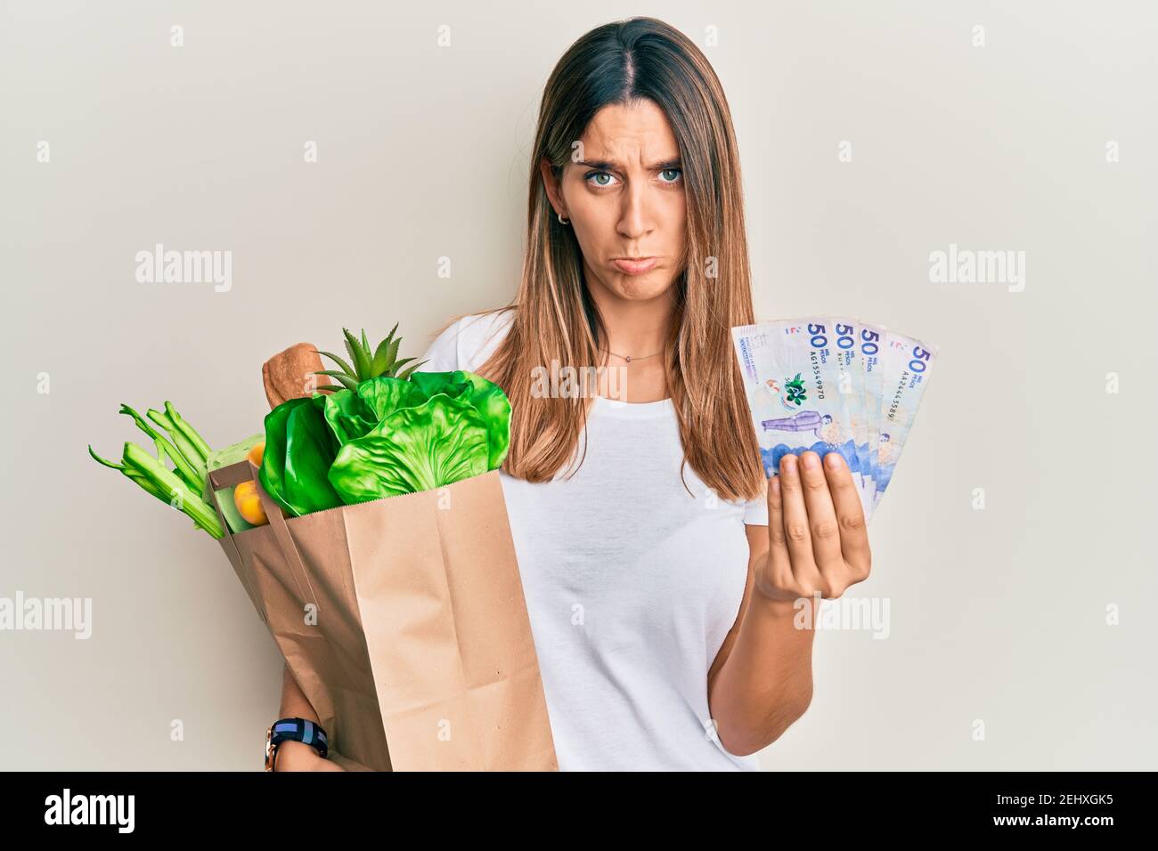 Brunette young woman holding groceries and 50 colombian pesos banknotes ...