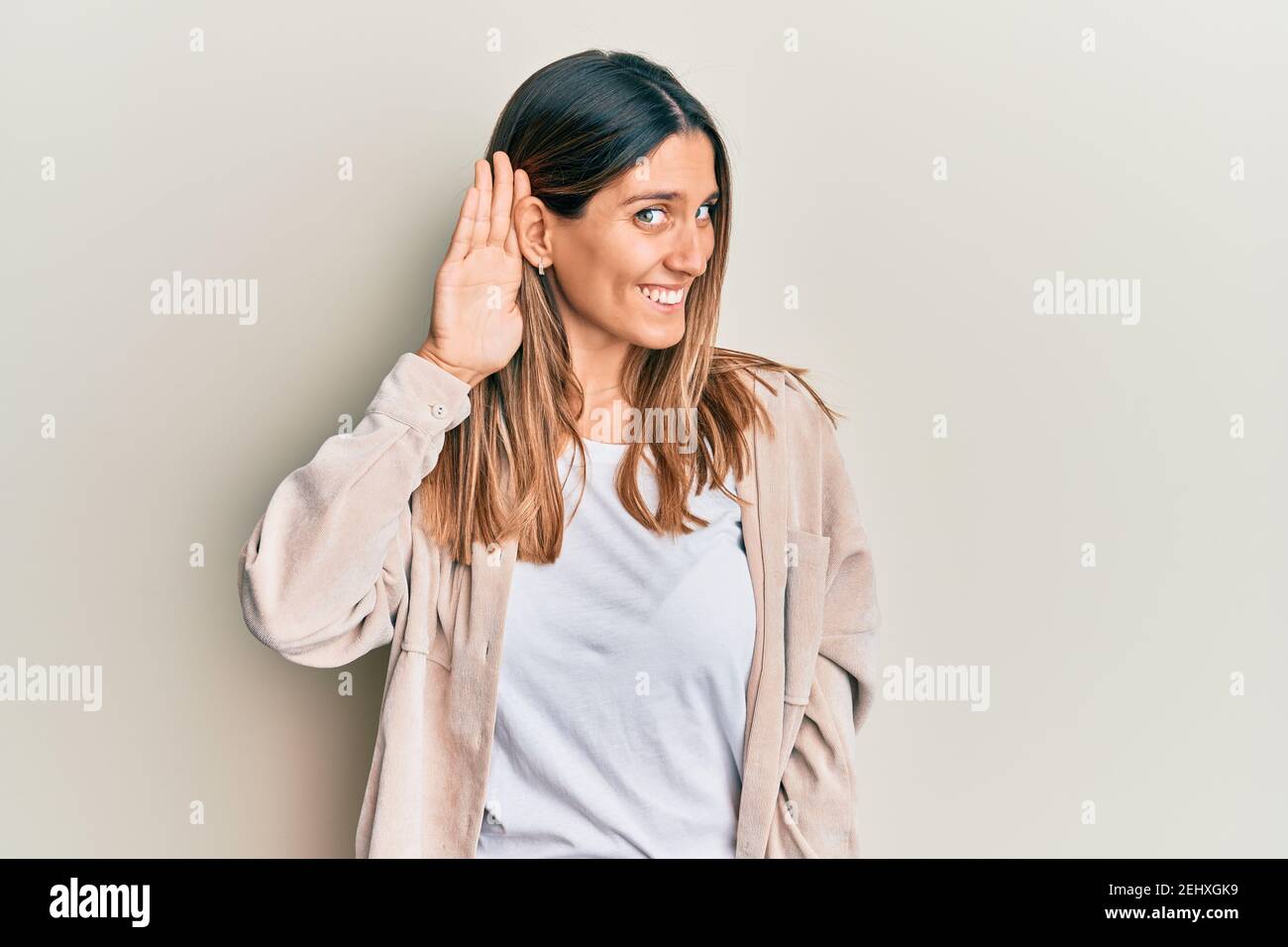 Brunette young woman wearing casual clothes smiling with hand over ear ...