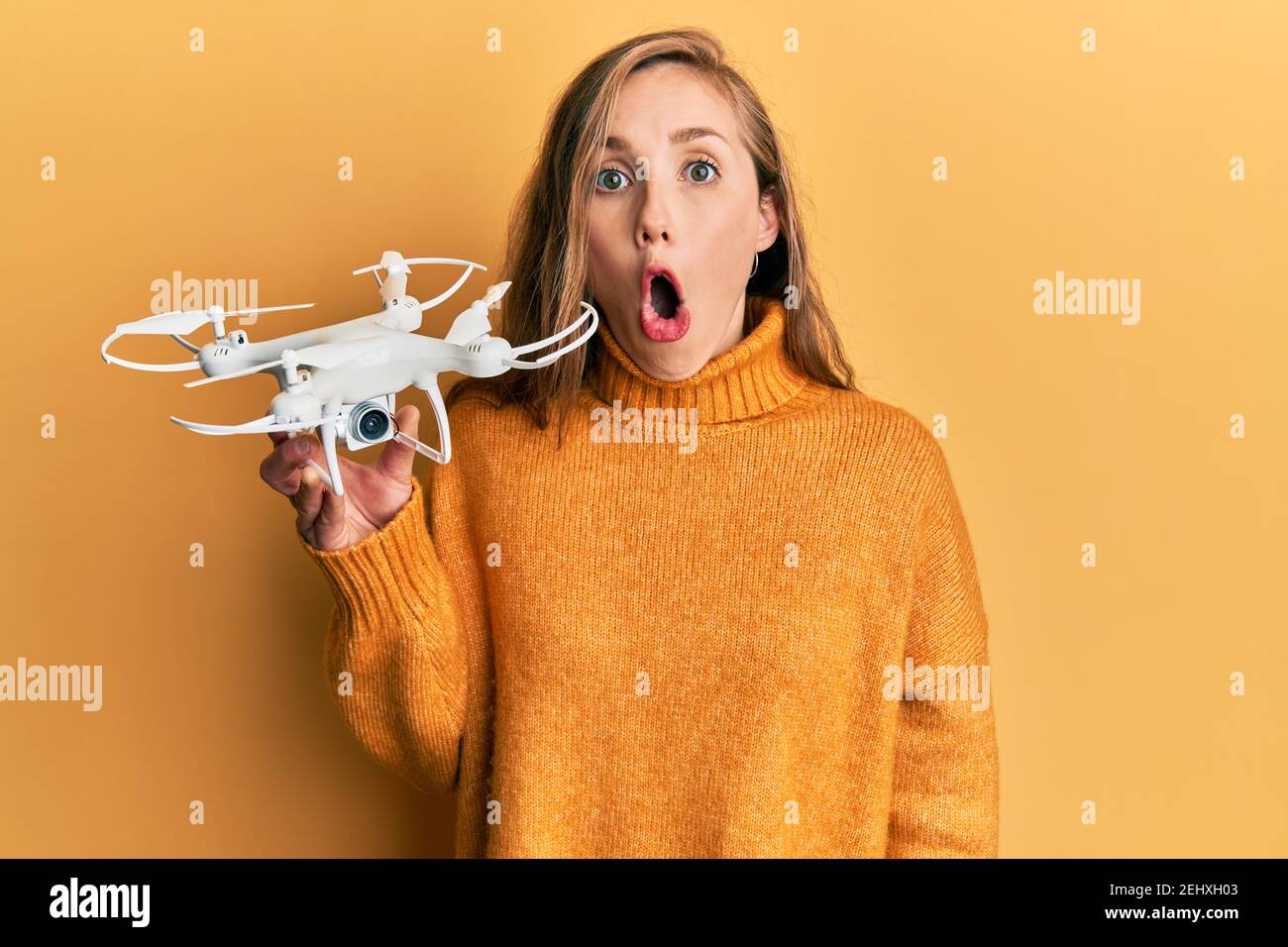 Young blonde woman holding drone scared and amazed with open mouth for ...
