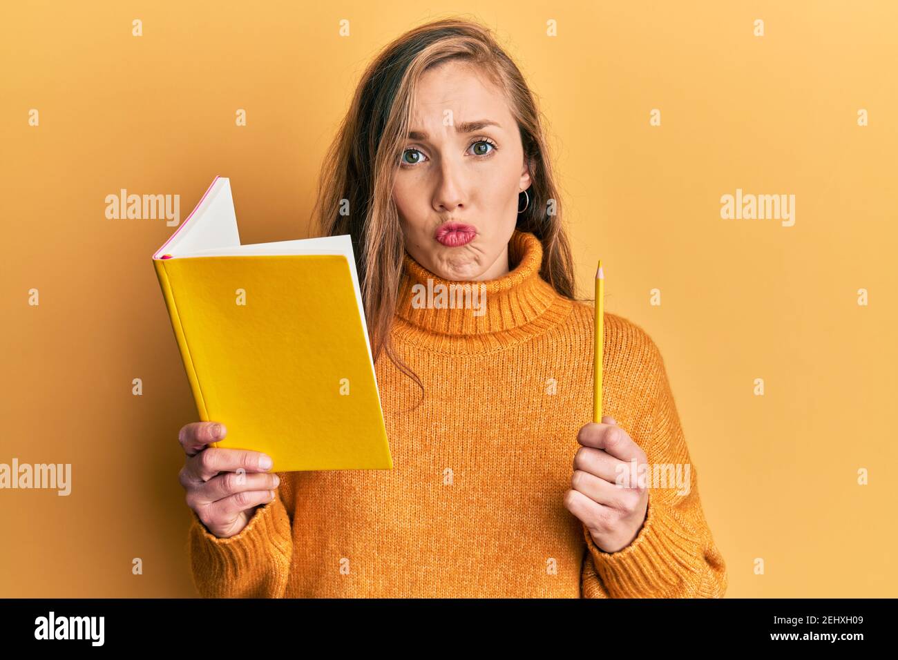 Young blonde woman holding book and pencil depressed and worry for ...