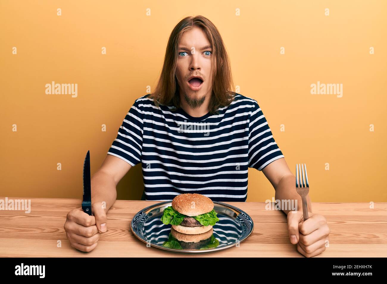 Handsome caucasian man with long hair eating a tasty classic burger ...