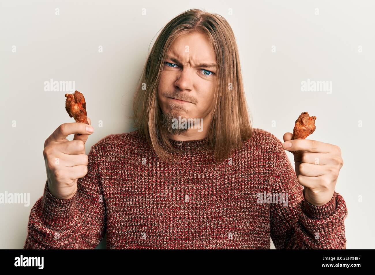 Handsome caucasian man with long hair eating chicken wings skeptic and ...