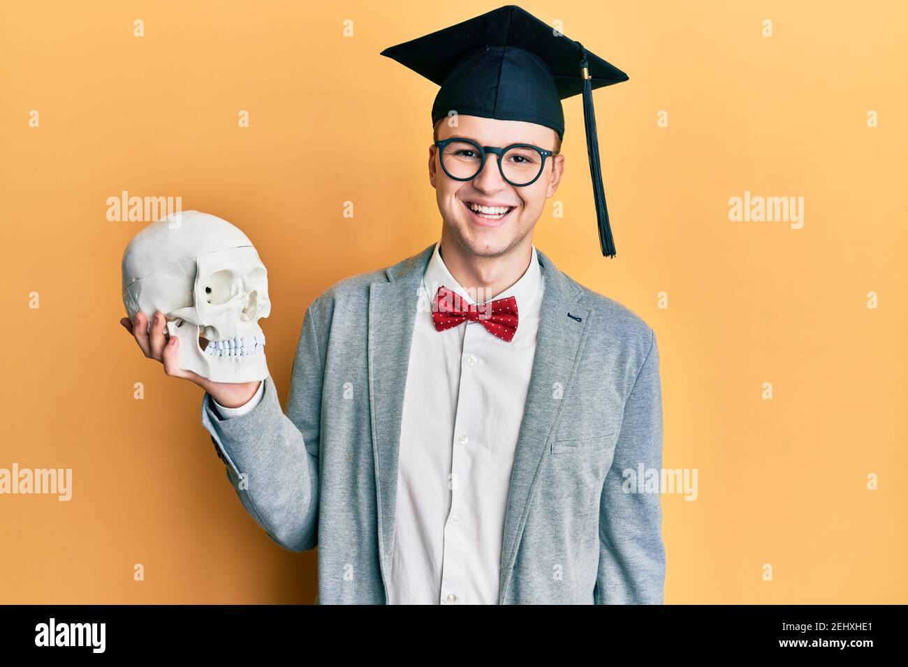 Young caucasian nerd man wearing glasses and graduation cap holding ...