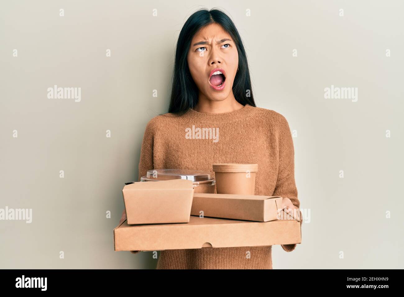 Young chinese woman holding take away food angry and mad screaming ...