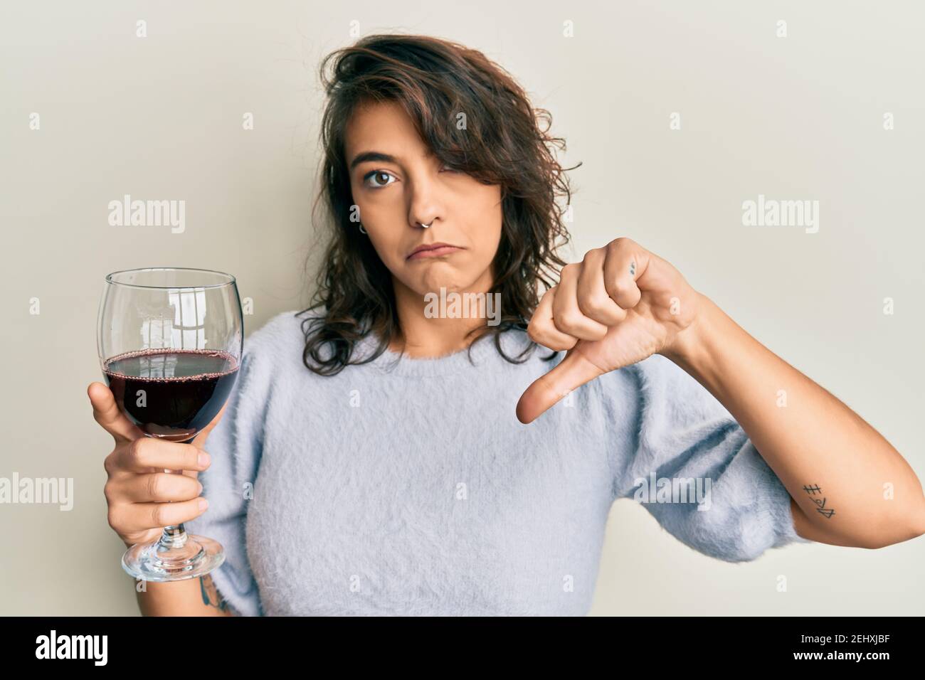 Young hispanic woman drinking a glass of red wine with angry face ...