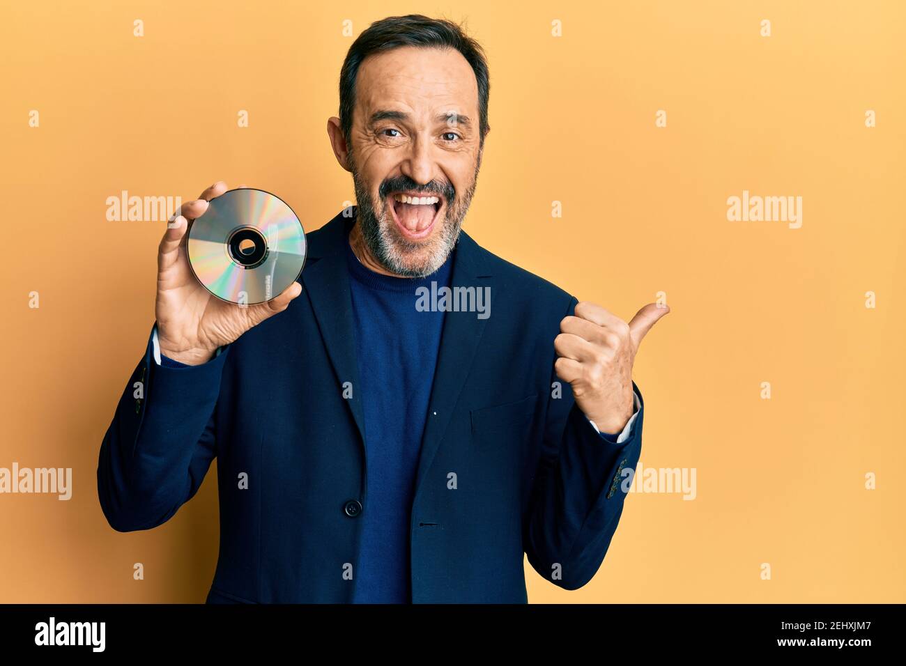 Middle age hispanic man holding compact disc pointing thumb up to the ...