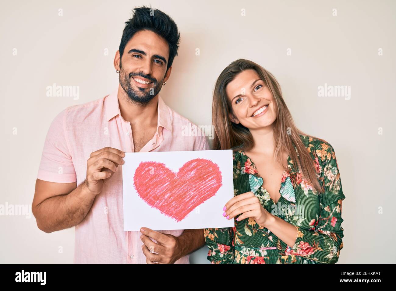 Beautiful young couple together holding heart draw smiling with a happy ...