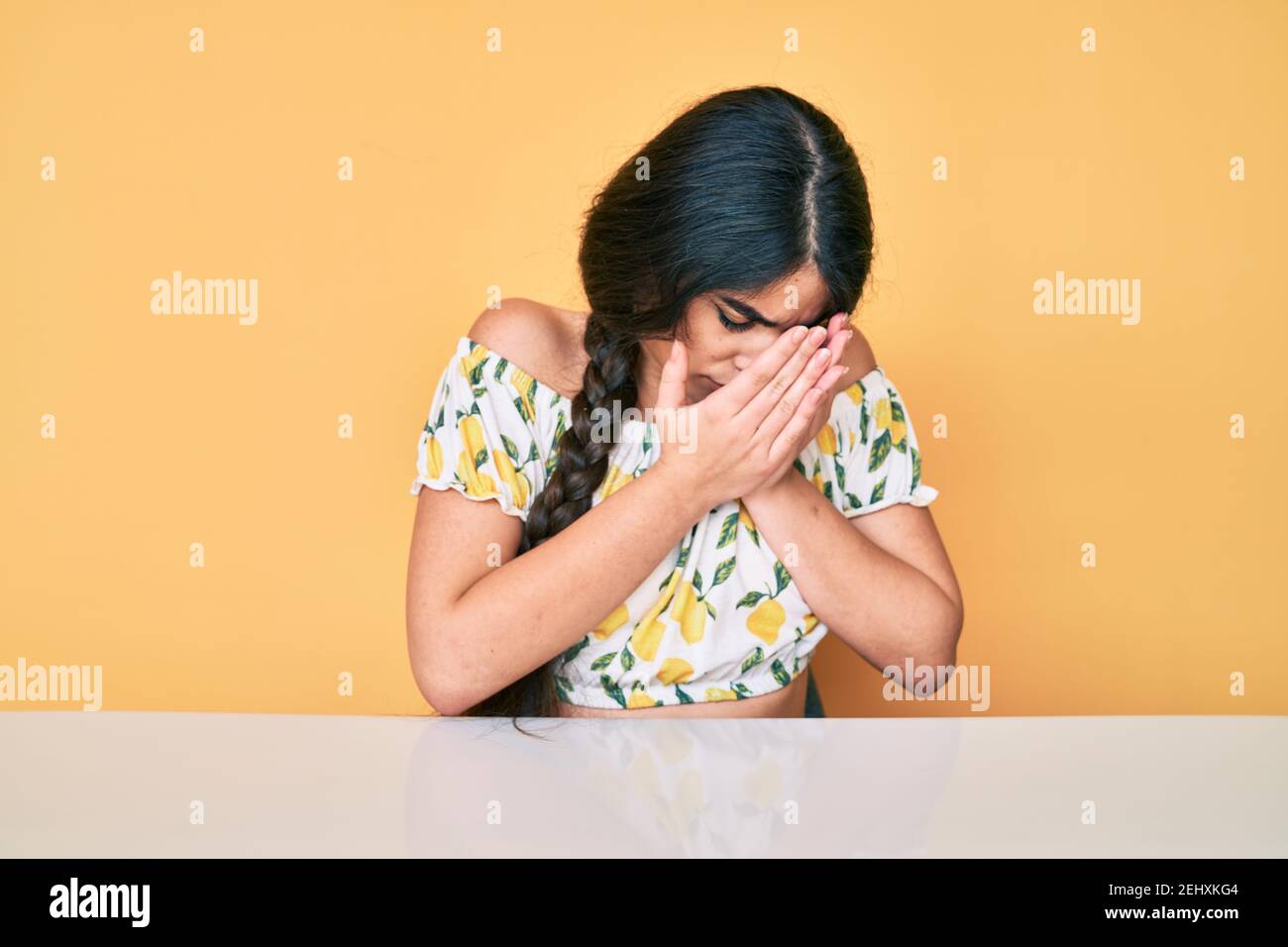 Brunette teenager girl wearing casual clothes sitting on the table with ...