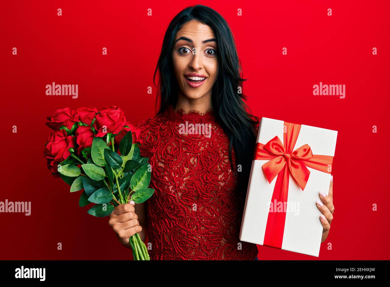 Beautiful hispanic woman holding anniversary gift and roses bouquet ...