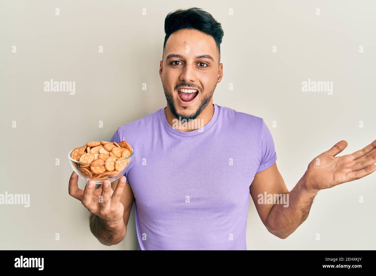 Young arab man holding bowl of salty crackers biscuits celebrating ...