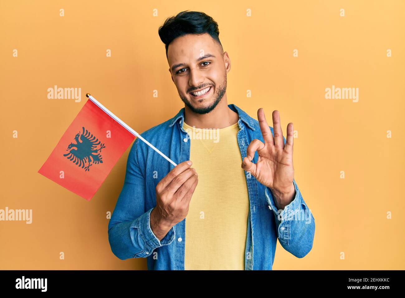 Young arab man holding albania flag doing ok sign with fingers, smiling ...