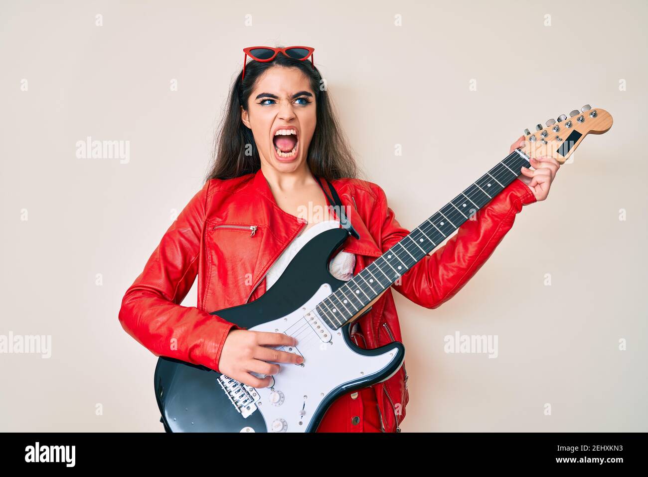 Brunette teenager girl playing electric guitar angry and mad screaming ...