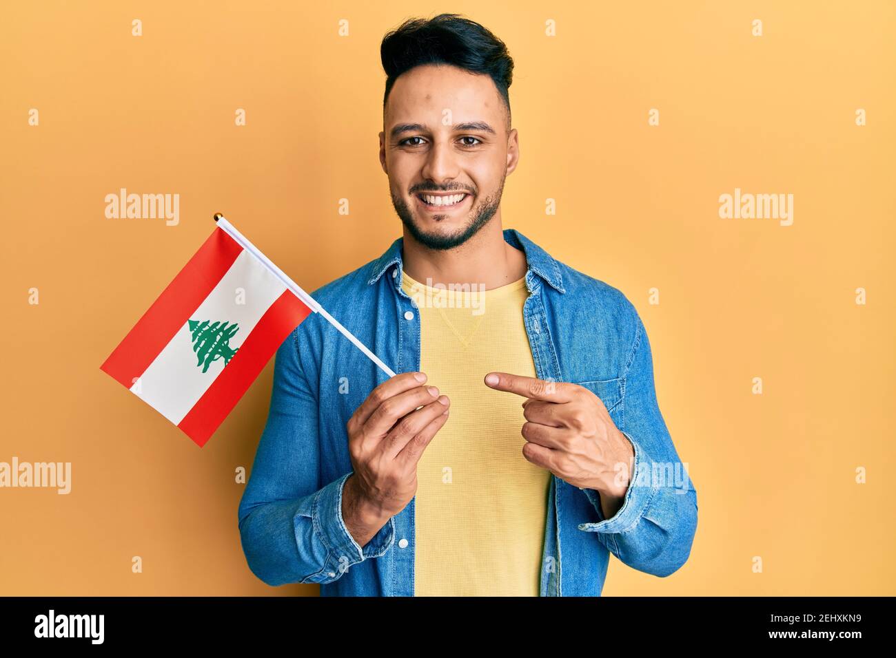 Young arab man holding lebanon flag smiling happy pointing with hand ...