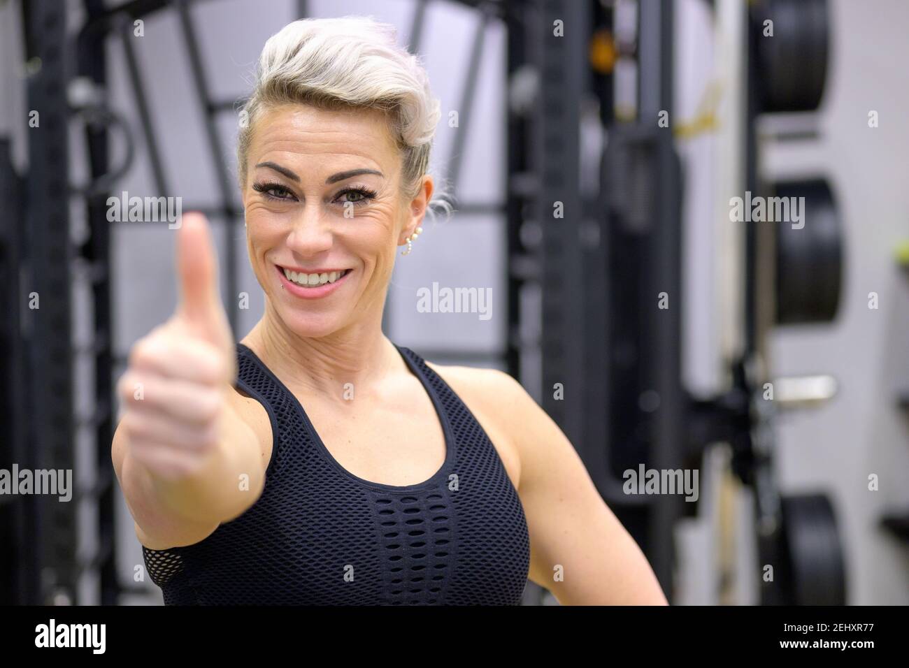Positive healthy fit woman giving a thumbs up gesture posing in front ...