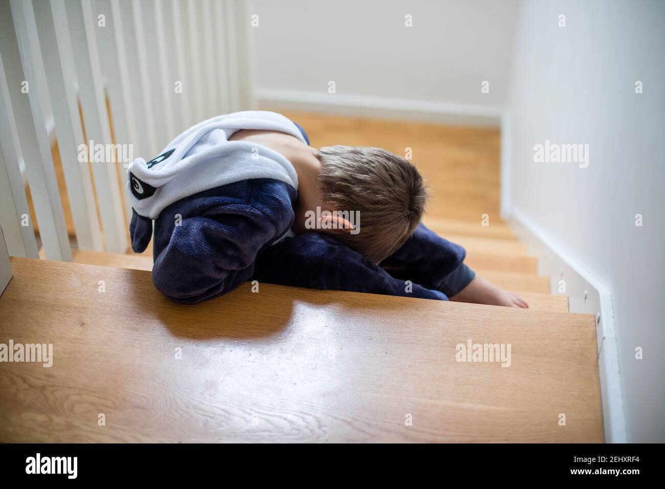 the unhappy child is sitting on the stairs with his head down Stock ...