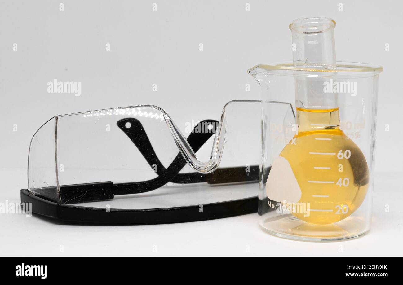 Yellow liquid in scientific beakers with safety glasses and a white ...