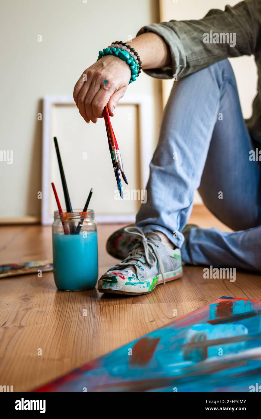 Artist woman holding paintbrush and sitting on floor after finished her ...