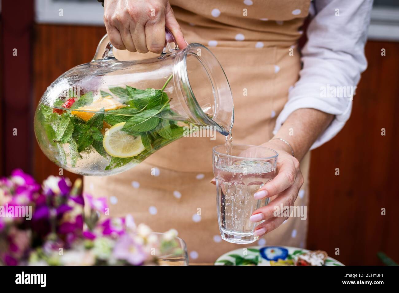 Woman pouring cold sparkling mineral water with mint herbs and lemon ...