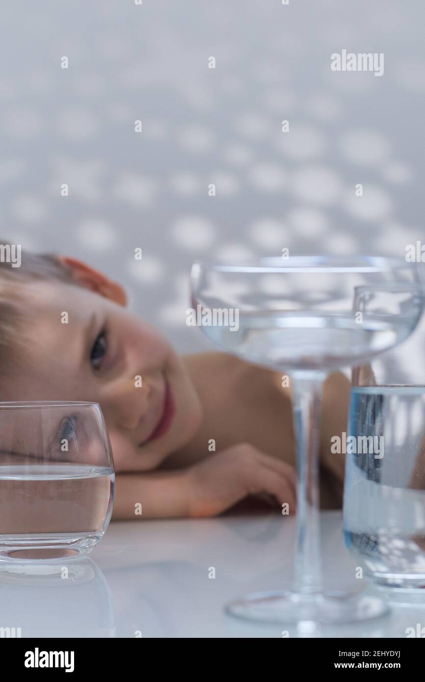 Portrait of a boy through glasses of water. Distorted glass of water ...