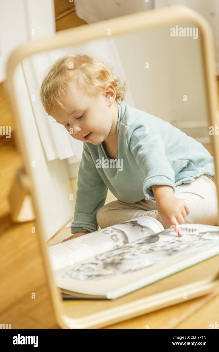 Vertical shot of a child reading a storybook visible in the mirror ...