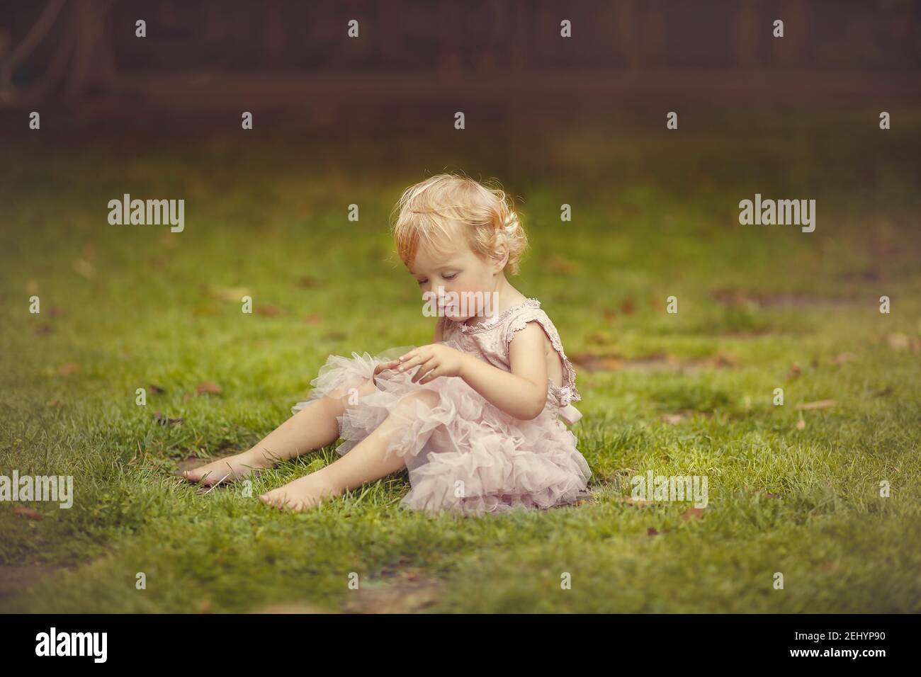 Cute child wearing a cute dress while sitting on a grass-covered meadow ...