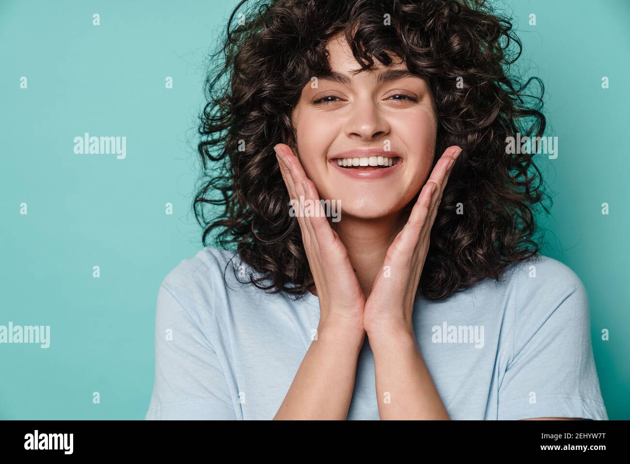 Joyful beautiful curly girl smiling and stroking her cheeks isolated ...