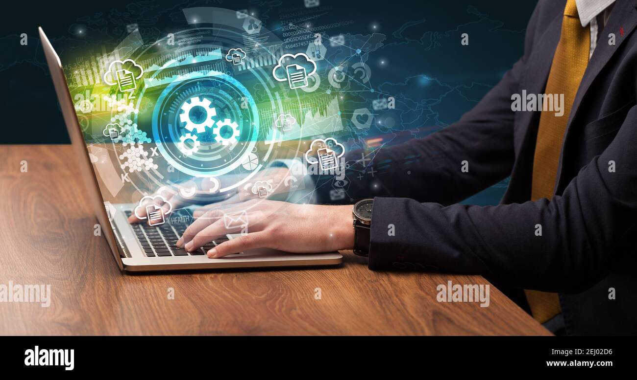 Business hand typing on a modern laptop with gear icon coming out from ...