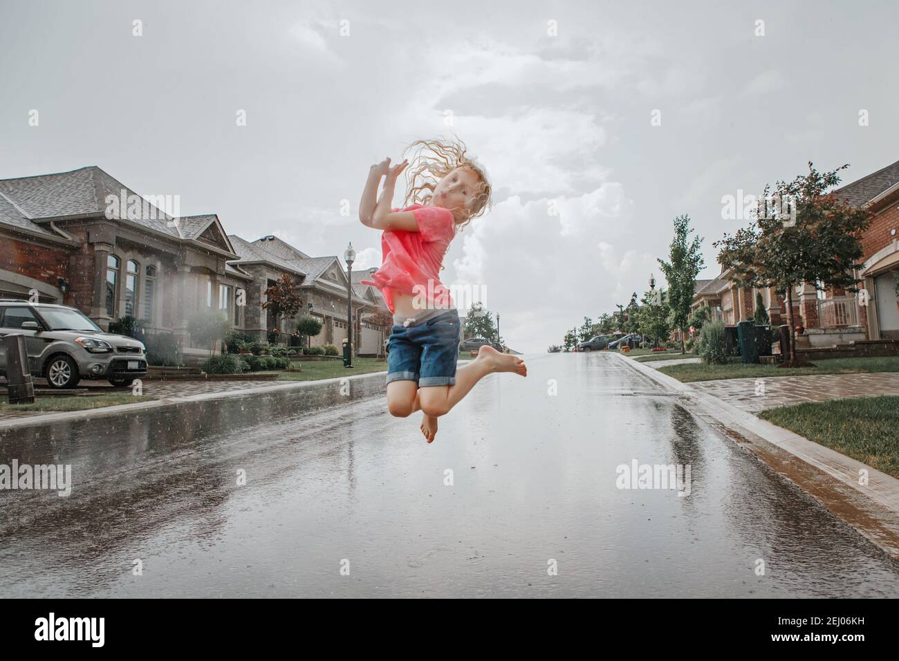 Cute adorable girl running splashing under rain on street road. Child ...