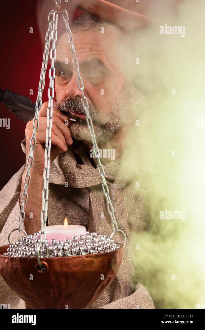 A monk sitting in smoke in front of a burning candle, holding a quill ...
